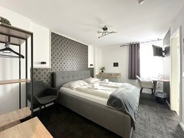 Quarto de hotel moderno com cama, escrivaninha, cadeira, televisão e guarda-roupa.