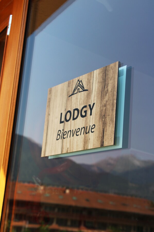 Uma placa de madeira com as palavras 'LODGY' e 'Bienvenue', indicando uma placa de boas-vindas, provavelmente em um estabelecimento de hospedagem.