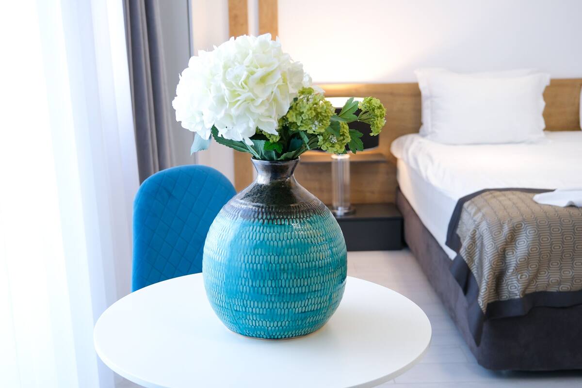 Um vaso azul-turquesa com flores brancas e verdes sobre uma mesa branca em um quarto de hotel.