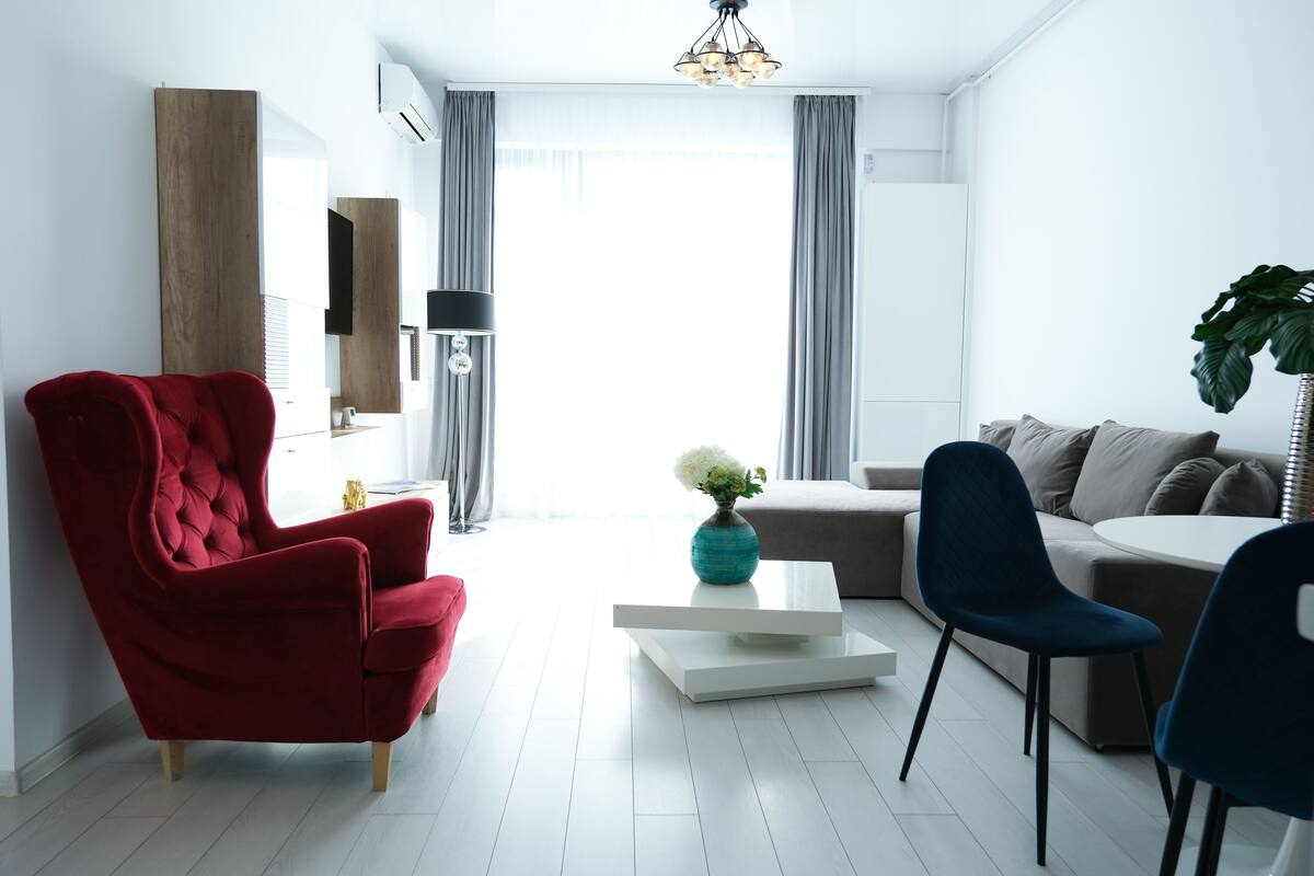 Uma sala de estar moderna com uma poltrona vermelha, uma cadeira azul, uma mesa de centro branca e um sofá bege.