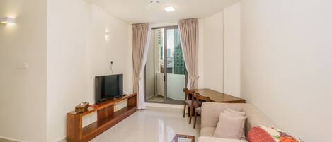 Uma sala de estar moderna com televisão de tela plana, mobiliário de madeira, uma mesa de centro de vidro e uma varanda com cortinas.
