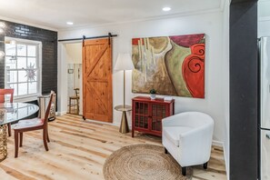Uma cozinha moderna com piso de madeira, uma mesa de jantar com cadeiras, um armário vermelho, uma poltrona branca e um quadro abstrato grande na parede.