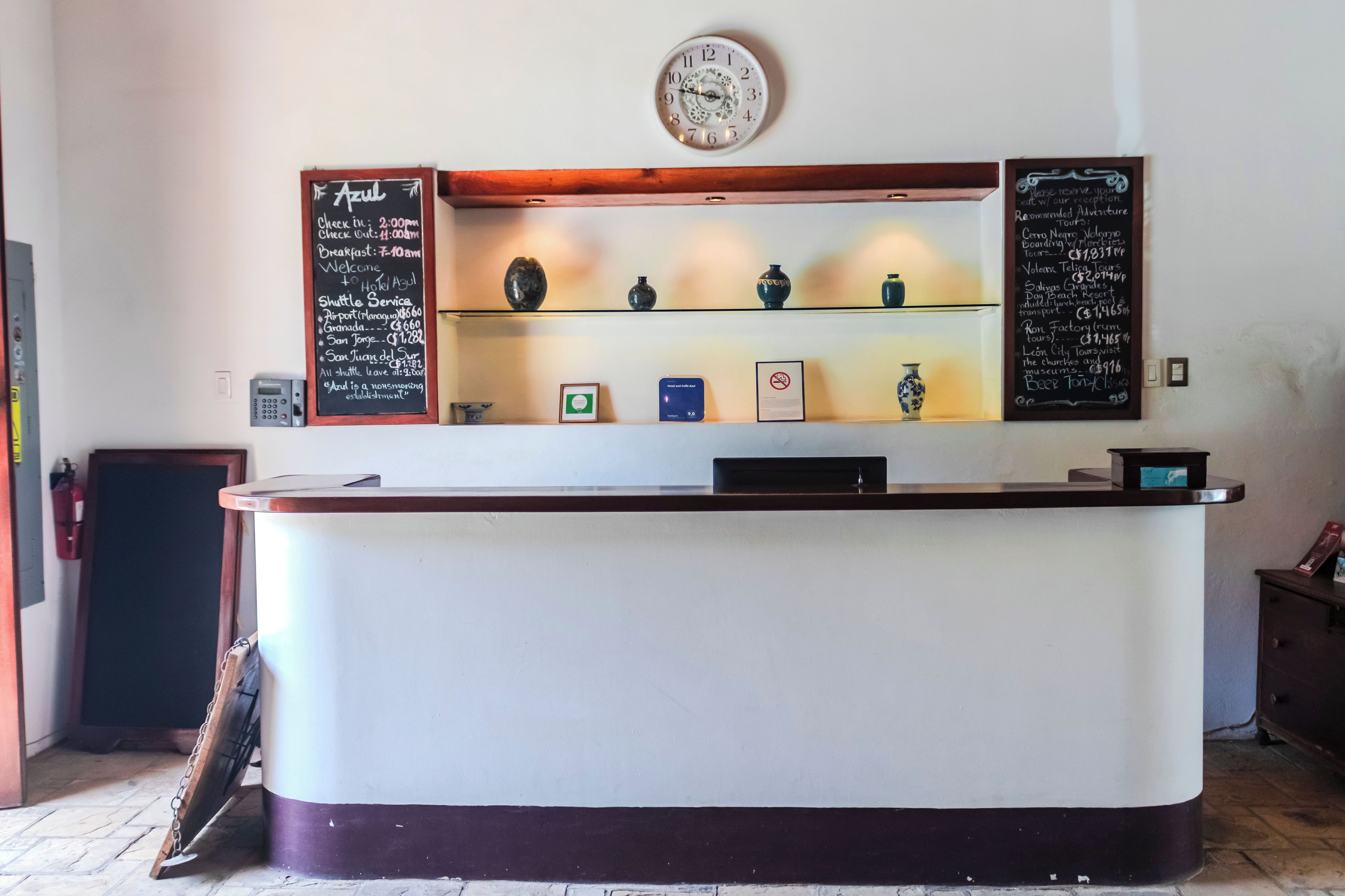 Uma mesa de recepção com um relógio, dois quadros-negros com texto e uma vitrine de vidro com vasos.