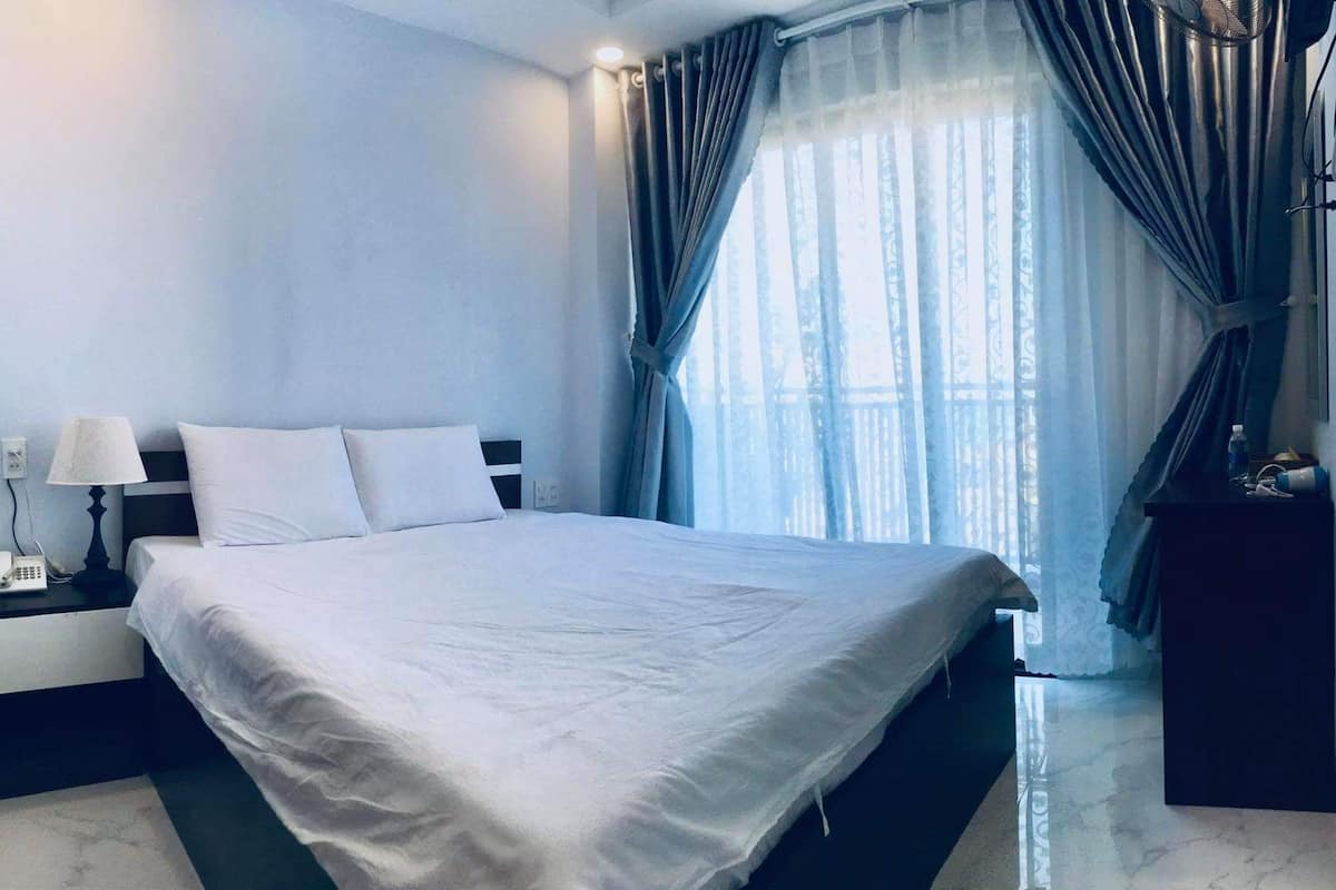 Quarto de hotel moderno com uma cama grande, uma mesa de cabeceira com abajur e um criado-mudo com telefone.