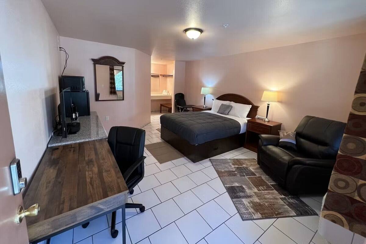 Quarto de hotel com cama, escrivaninha, cadeira e uma pequena área de cozinha.