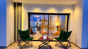 Uma área moderna para sentar ao ar livre, com duas cadeiras verdes e almofadas, e uma pequena mesa, com vista para uma piscina e zona de refeições ao ar livre.