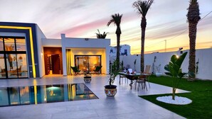Uma casa moderna com piscina, área de estar externa e palmeiras.