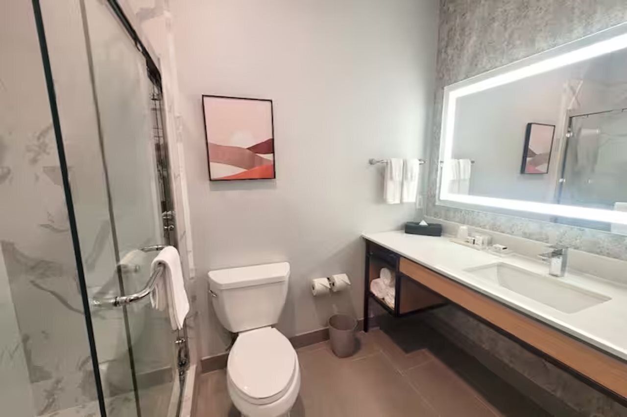 Um banheiro moderno com box de vidro, vaso sanitário, pia com espelho grande e porta-toalhas.