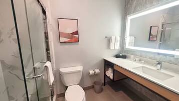 Um banheiro moderno com box de vidro, vaso sanitário, pia com espelho grande e porta-toalhas.