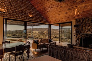 Um quarto espaçoso com uma grande mesa de jantar, um sofá e uma lareira. O quarto possui janelas amplas que oferecem vista para o exterior.
