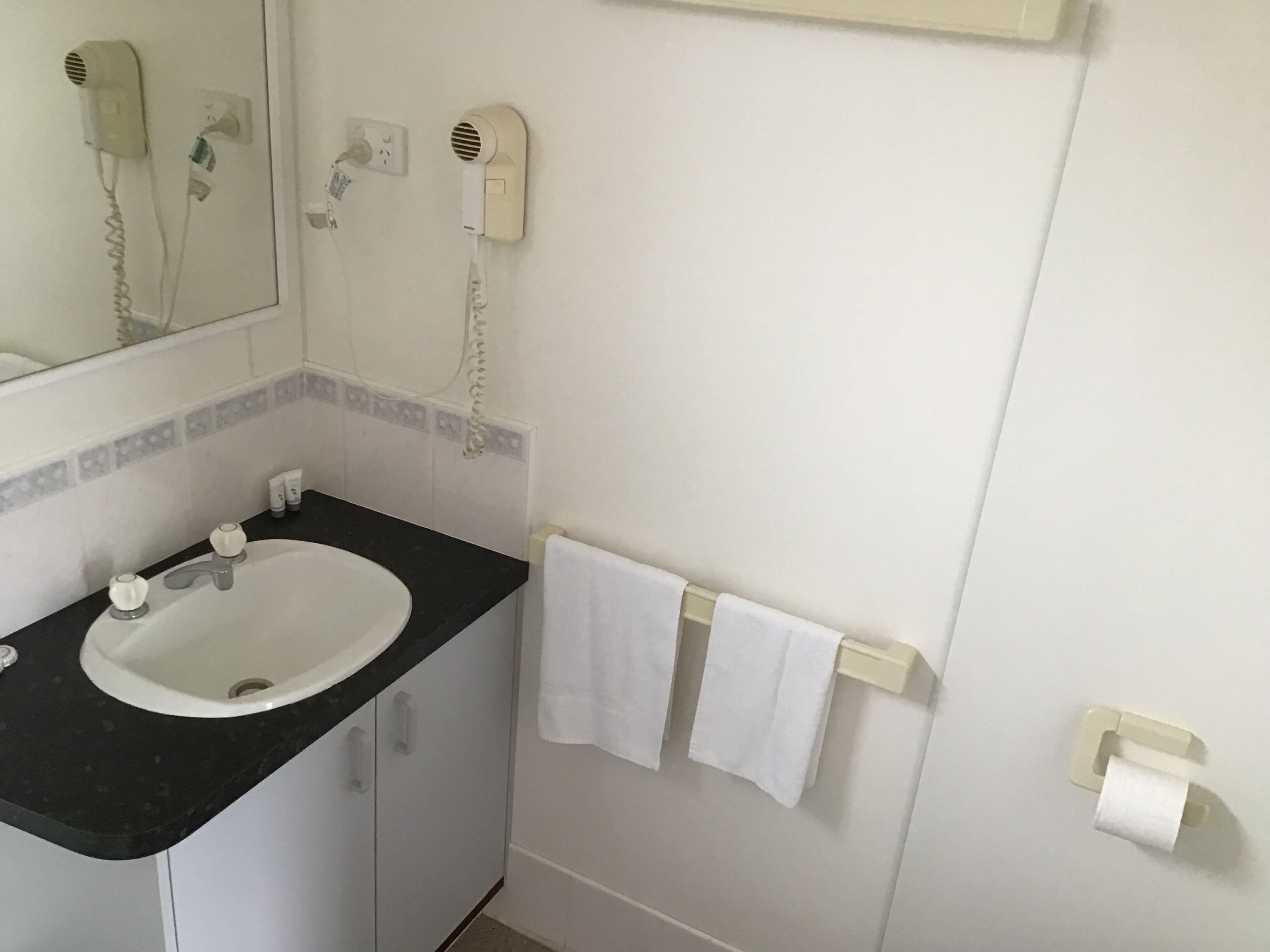 Uma casa de banho com lavatório, espelho, secador de cabelo e porta-toalhas.