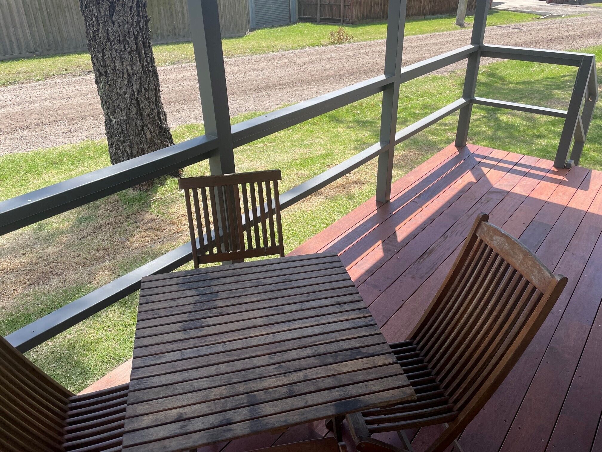Um deck de madeira com mesa e cadeiras, rodeado por um corrimão de metal.