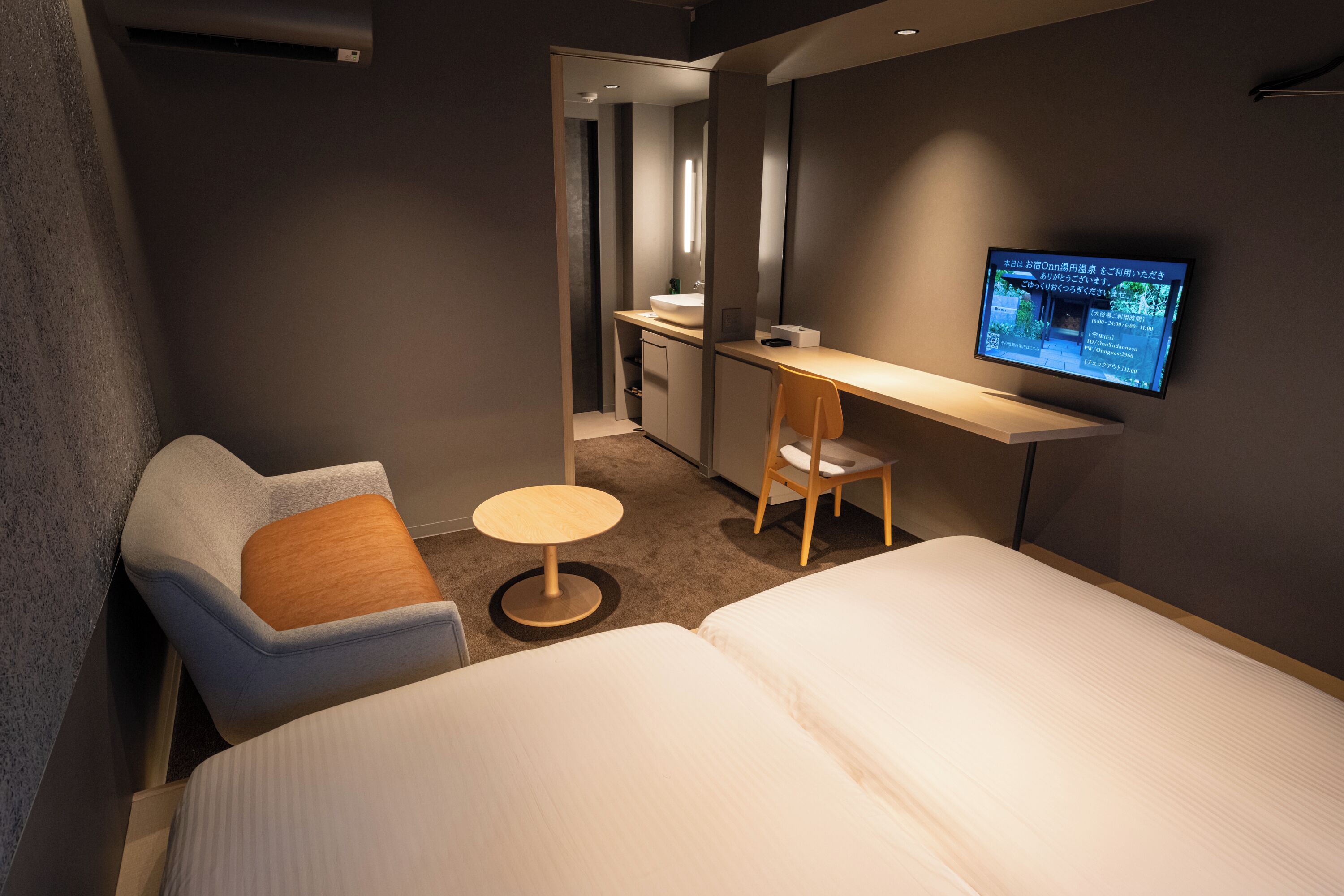Quarto de hotel com cama, escrivaninha, cadeira e televisão.