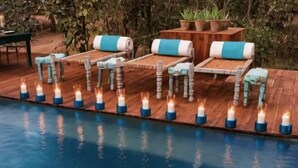 Uma área à beira da piscina com espreguiçadeiras de madeira e uma fileira de velas.