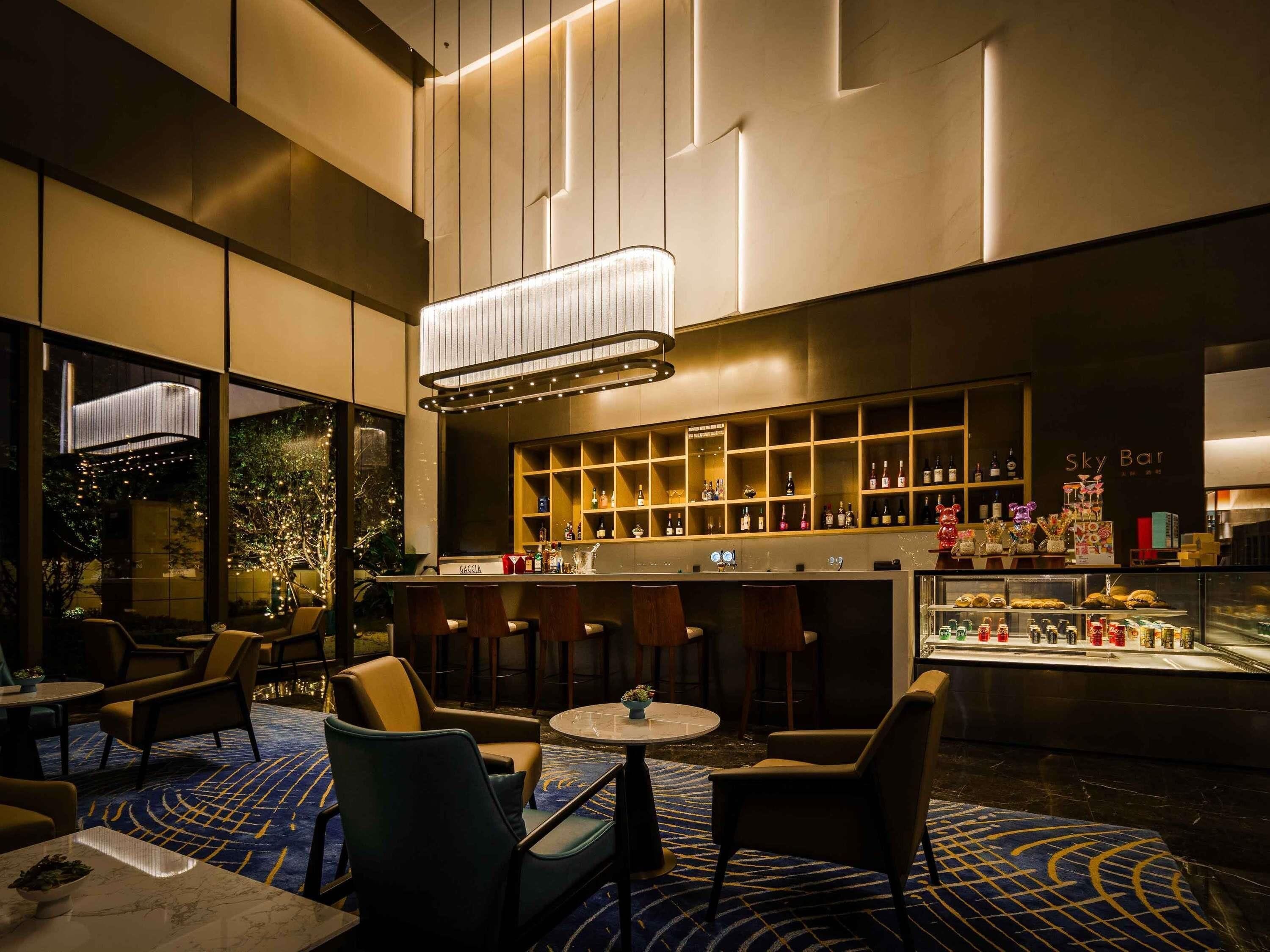Uma área de bar com balcão, prateleiras com garrafas e um expositor com alimentos.