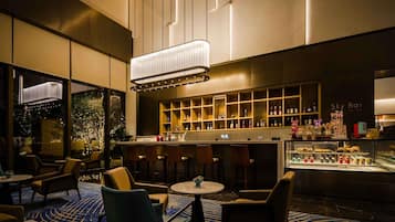 Uma área de bar com balcão, prateleiras com garrafas e um expositor com alimentos.