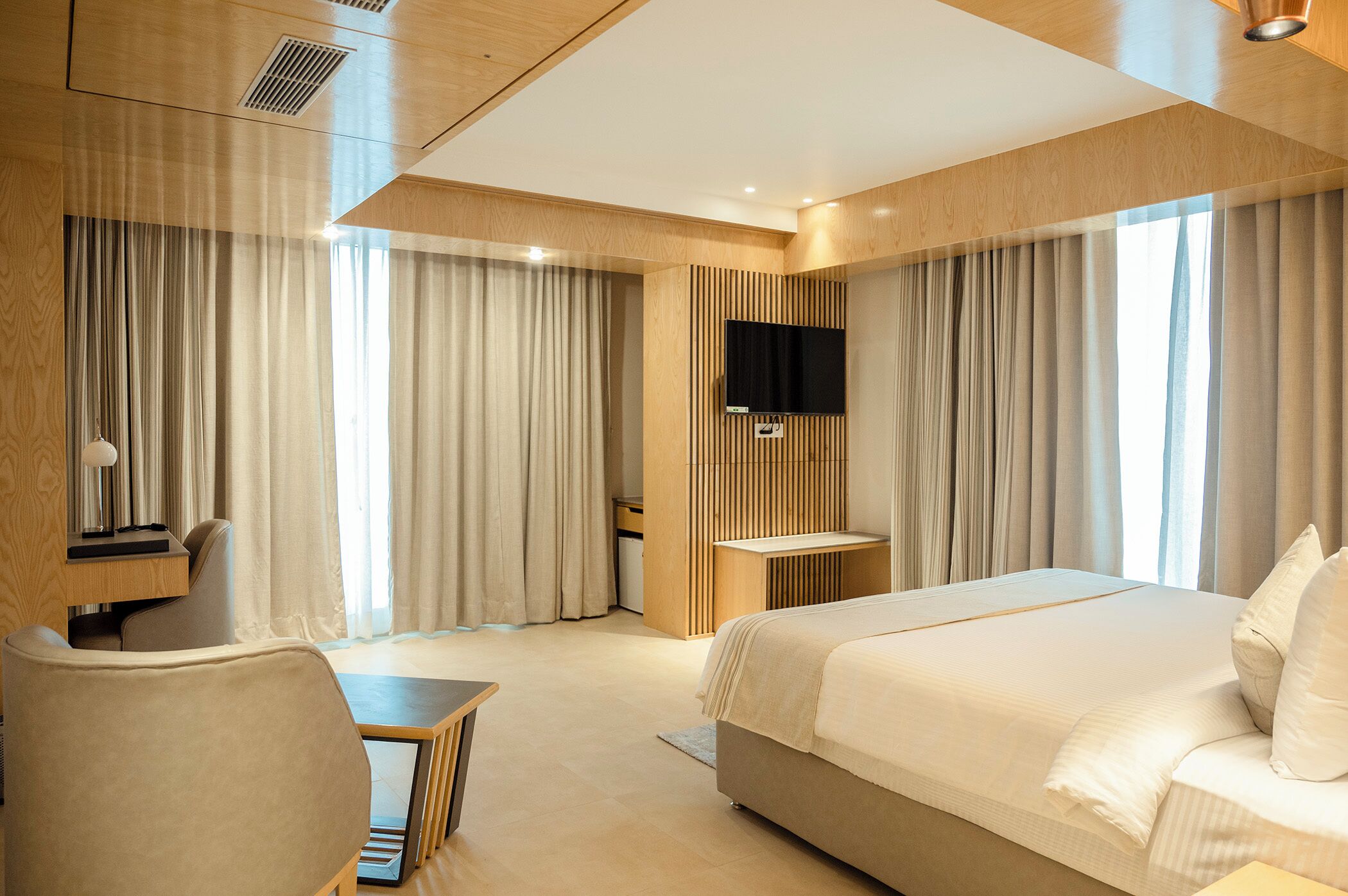 Quarto de hotel moderno com uma cama grande, uma escrivaninha e uma TV fixada na parede.