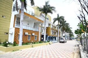 Edifício de vários andares com fachada de tijolos e paredes brancas, entrada visível e calçada pavimentada.