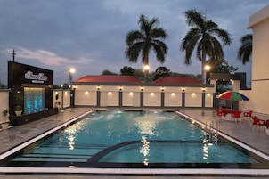 Uma piscina com uma fonte, rodeada por palmeiras e um edifício com telhado vermelho.