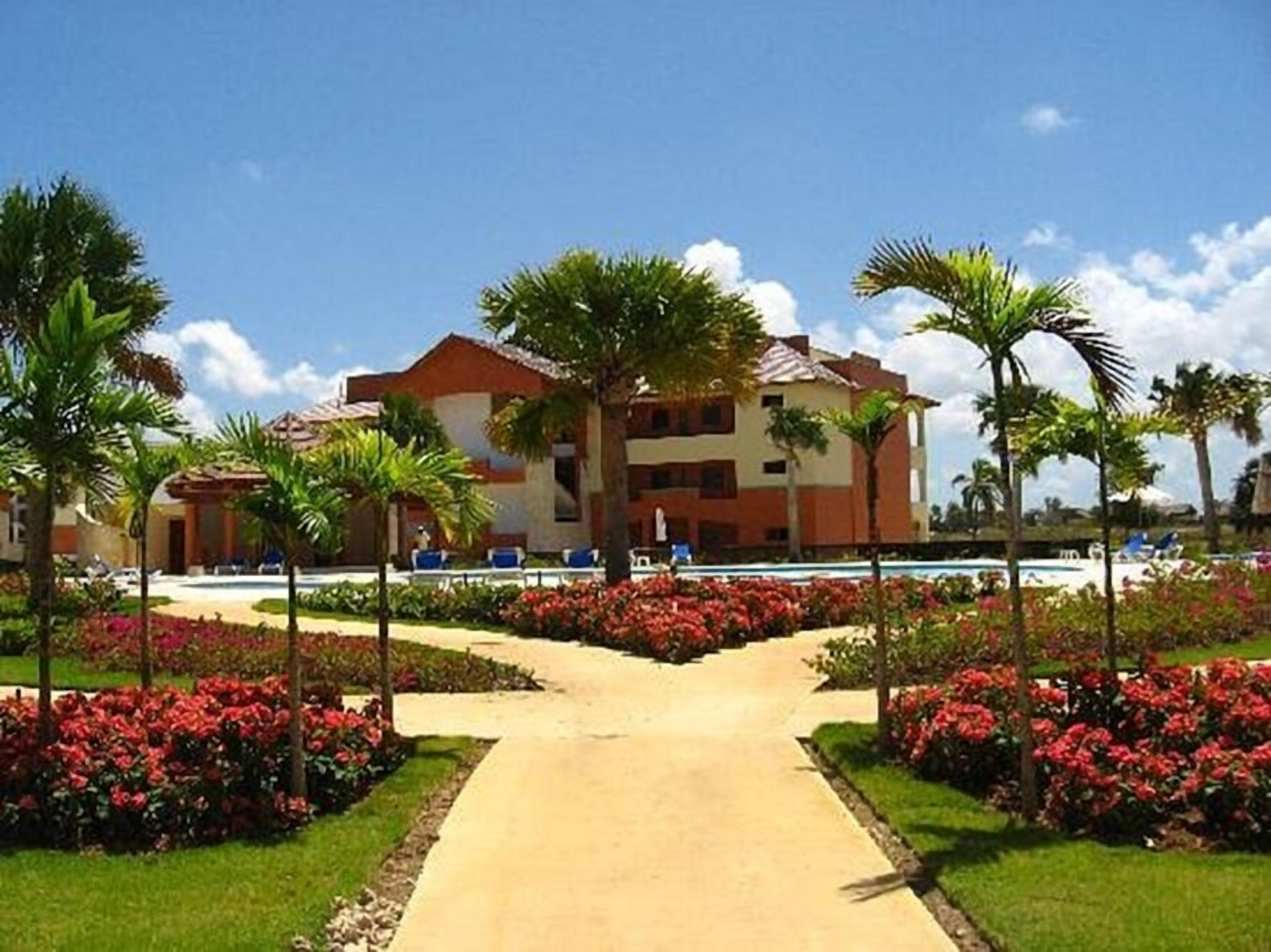 Um hotel com um pátio central, palmeiras e flores vermelhas.