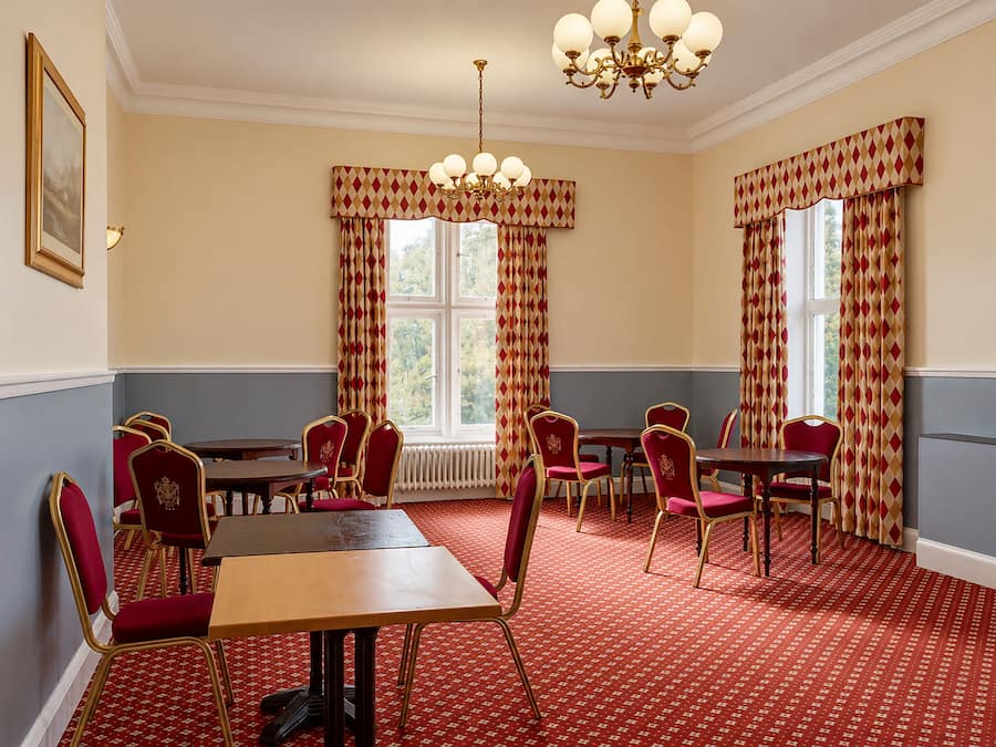 Quarto com carpete vermelho, um candelabro e cortinas com padrão em vermelho e dourado.