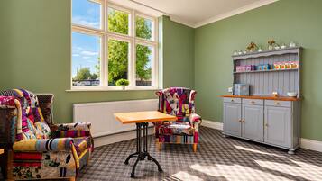 Um quarto com janela, duas cadeiras, uma mesa e um armário.