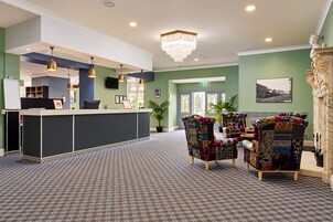 Uma área de recepção com balcão de check-in, um candelabro e duas poltronas estampadas.