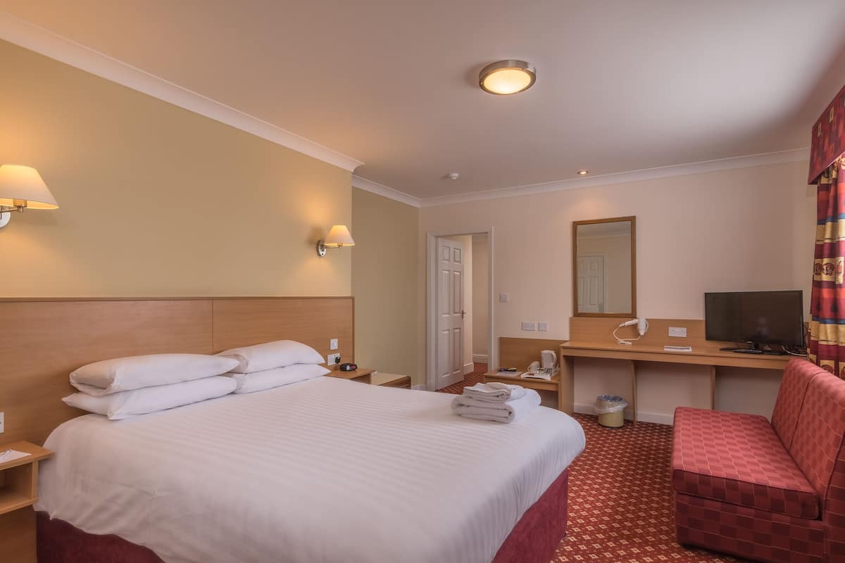 Quarto de hotel com uma cama grande, uma escrivaninha com computador, uma cadeira e uma televisão.