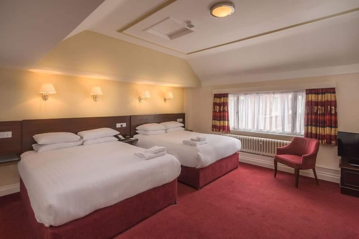 Quarto de hotel com duas camas, um tapete vermelho, uma cadeira e uma televisão.