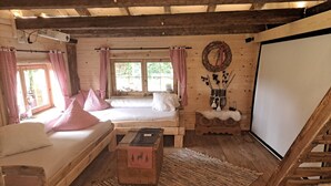 Um quarto de cabana aconchegante, com uma cama, um banco de madeira, uma pequena mesa e uma tela de projetor.