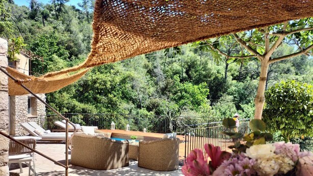 Um pátio com móveis de vime, piscina e vista para uma área arborizada.