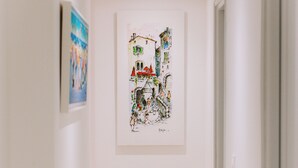 Um corredor com uma obra de arte emoldurada na parede, uma porta à direita e uma escadaria no final.
