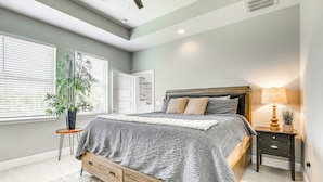 Quarto com cama grande, mesas de cabeceira, um criado-mudo, planta em vaso e janela com persianas.