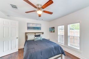 Quarto com cama, ventilador de teto, janela com persianas e porta.