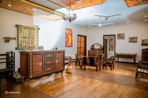 Um quarto amplo com piso de madeira, um armário grande de madeira, uma mesa de jantar com cadeiras e um ventilador de teto.