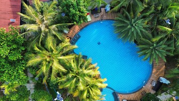 Vista aérea de uma piscina cercada por vegetação exuberante e palmeiras.
