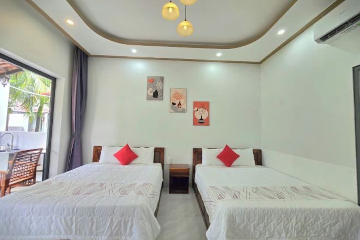 Quarto de hotel com duas camas, uma escrivaninha e uma janela.