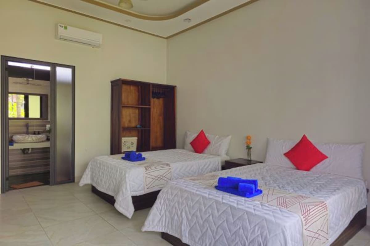 Quarto de hotel com duas camas, um guarda-roupa e casa de banho com espelho.