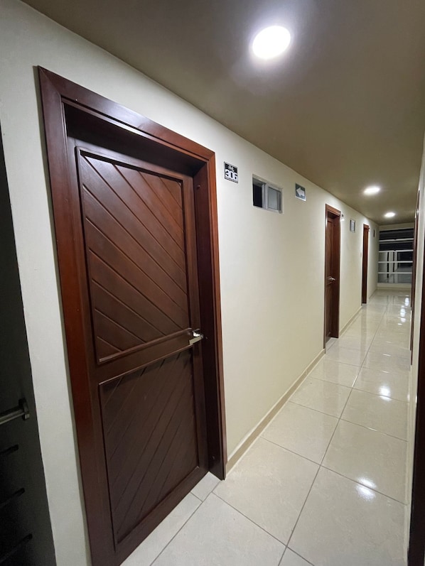 Corredor com portas de madeira, piso de azulejos e uma luminária no teto.