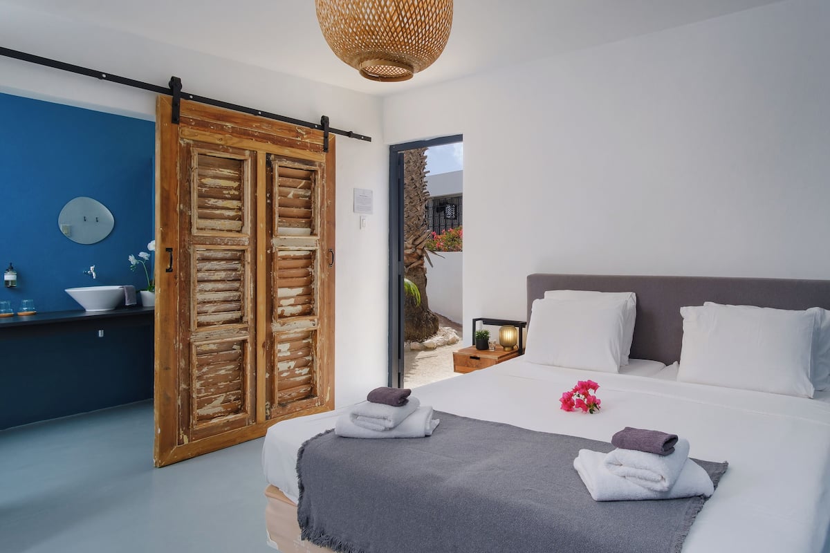Quarto com uma cama grande, banheiro com parede azul e porta de madeira.