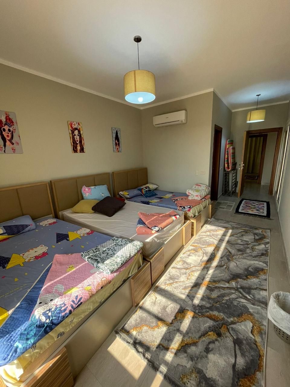 Quarto de hotel com duas camas, uma janela grande, ventilador de teto e ar condicionado fixado na parede.