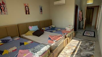 Quarto de hotel com duas camas, uma janela grande, ventilador de teto e ar condicionado fixado na parede.