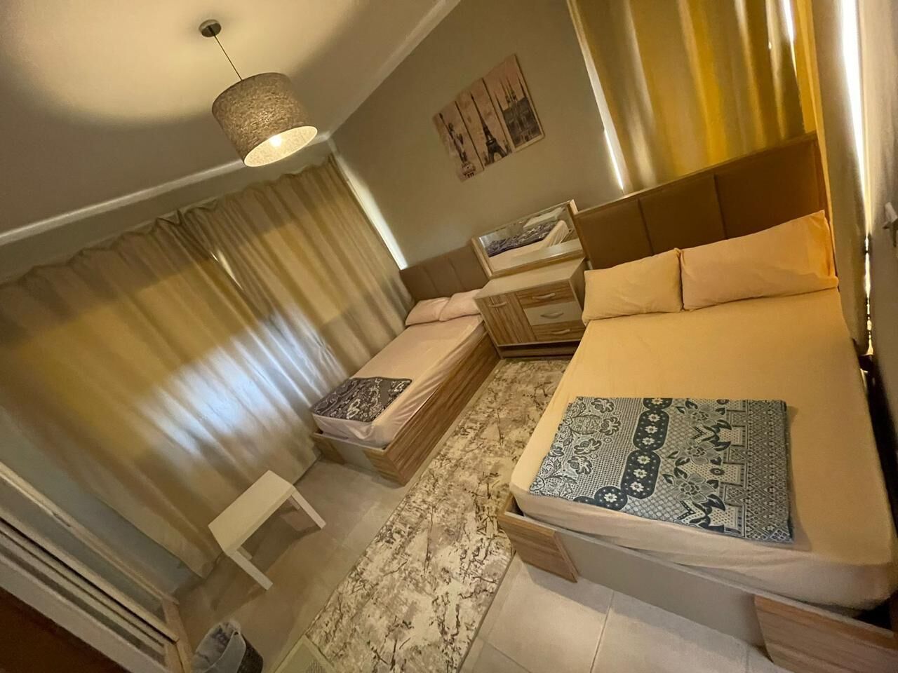 Quarto compacto com duas camas de solteiro, uma pequena escrivaninha e luminária suspensa.