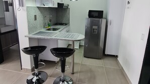 Uma cozinha moderna com uma ilha central, dois banquetes, uma geladeira e um micro-ondas.