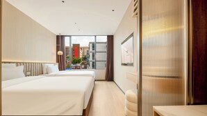 Quarto de hotel moderno com duas camas grandes, piso de madeira, uma janela ampla com vista para prédios e um espelho grande.