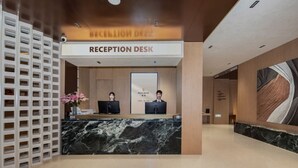 Bancada de recepção em mármore, dois recepcionistas e uma placa indicando a área de recepção.