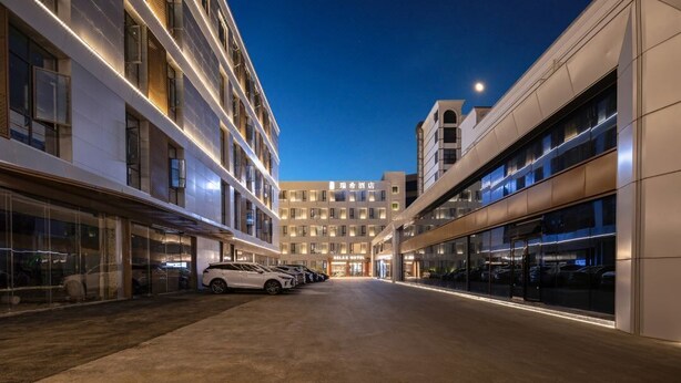 Um hotel moderno com um pátio central, vários andares e fachada bem iluminada.