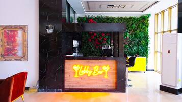 Um lobby com balcão de recepção, uma placa de neon que diz "Lobby Bar", um quadro emoldurado e uma parede verde com plantas.