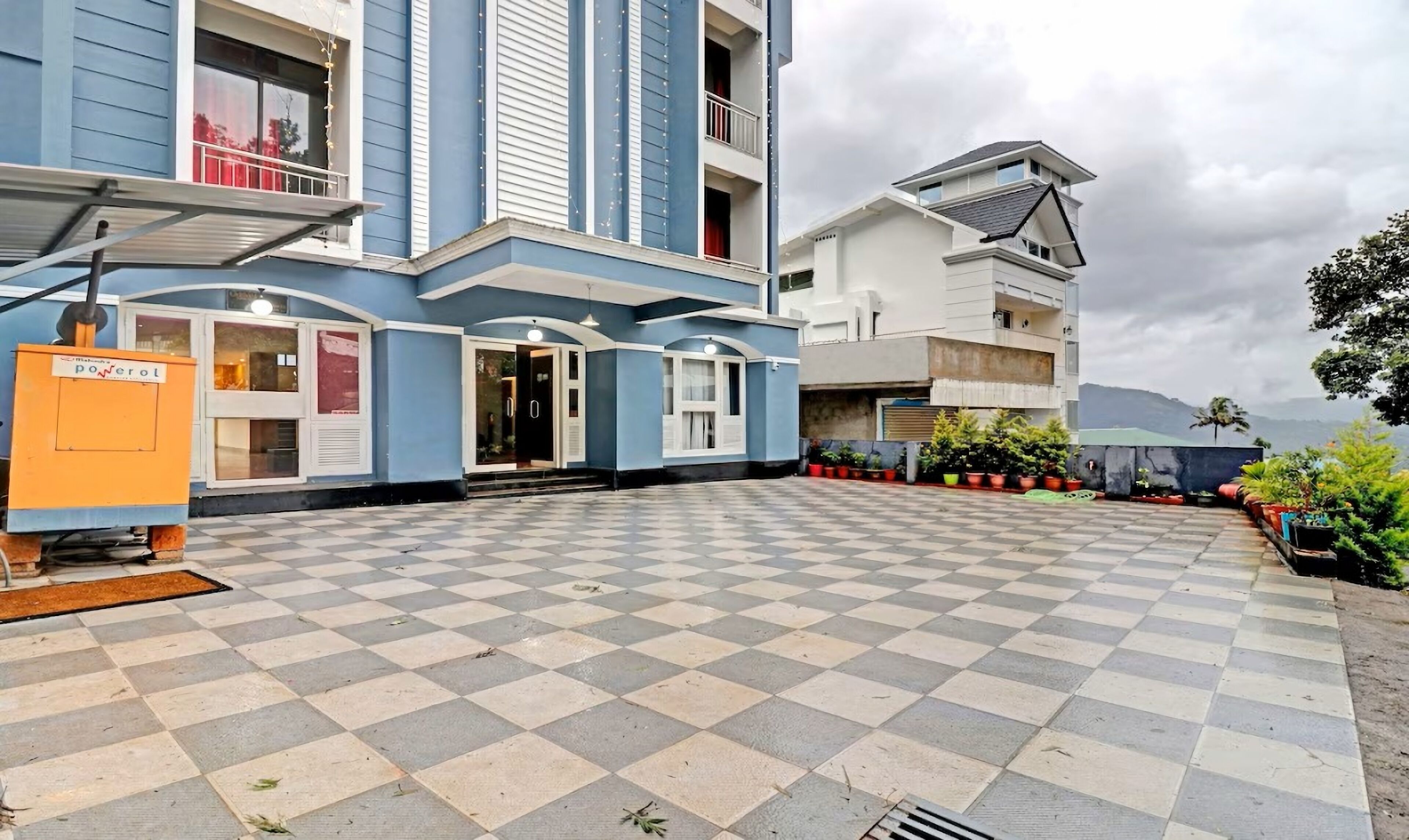 Um edifício com fachada azul e branca, um pátio com ladrilhos xadrez e vasos de plantas.