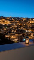 Uma cidade em declive, densamente povoada, ao entardecer, com edifícios iluminados e uma cúpula imponente.